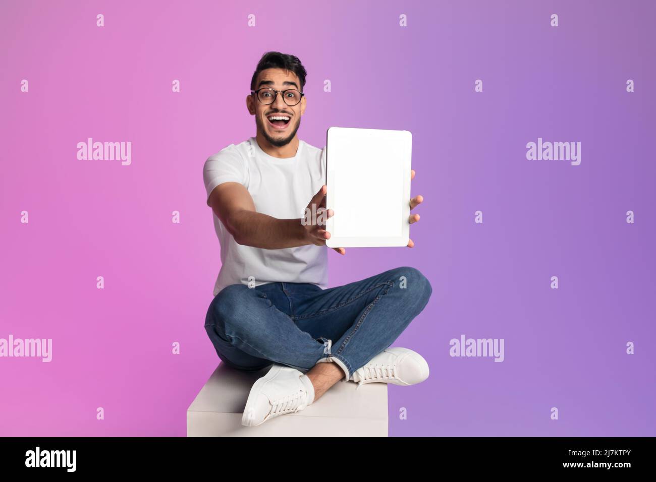 Excited millennial Arab man showing tablet with blank screen in neon ...