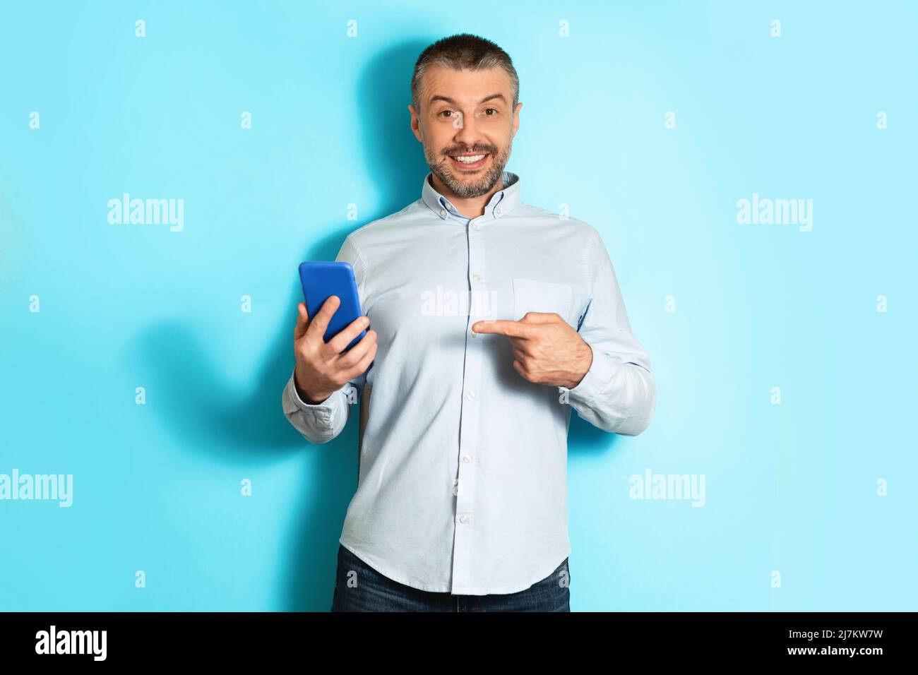 Middle Aged Male Pointing At Phone Advertising App, Blue Background ...