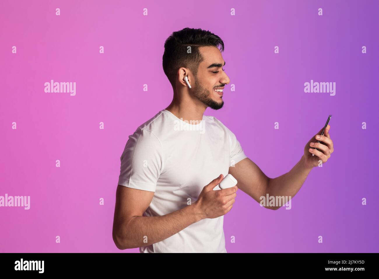 Happy young Arab guy with smartphone listening to music in wireless ...