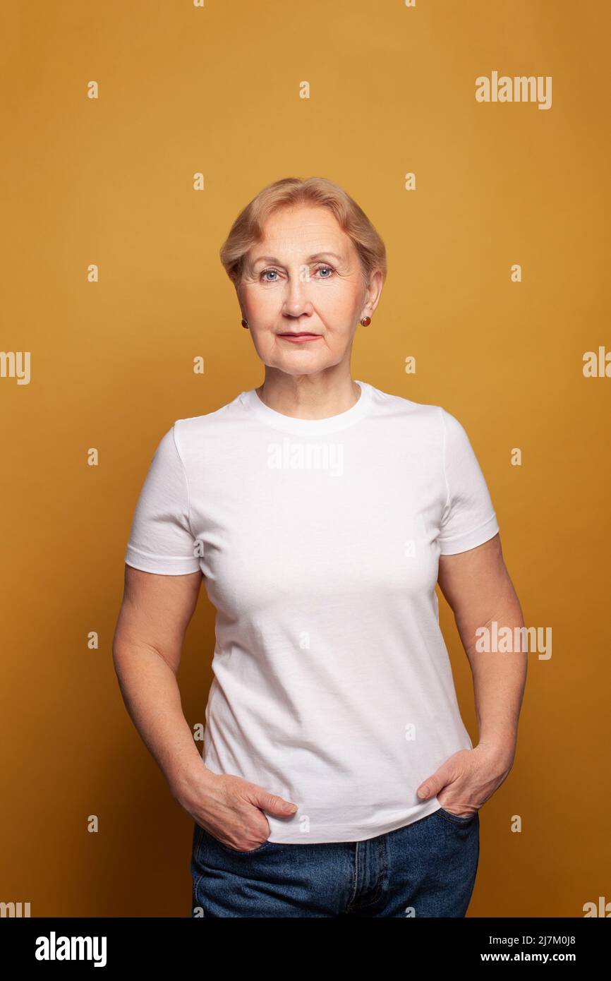 Mature woman in white t-shirt on bright yellow studio wall background Stock Photo - Alamy