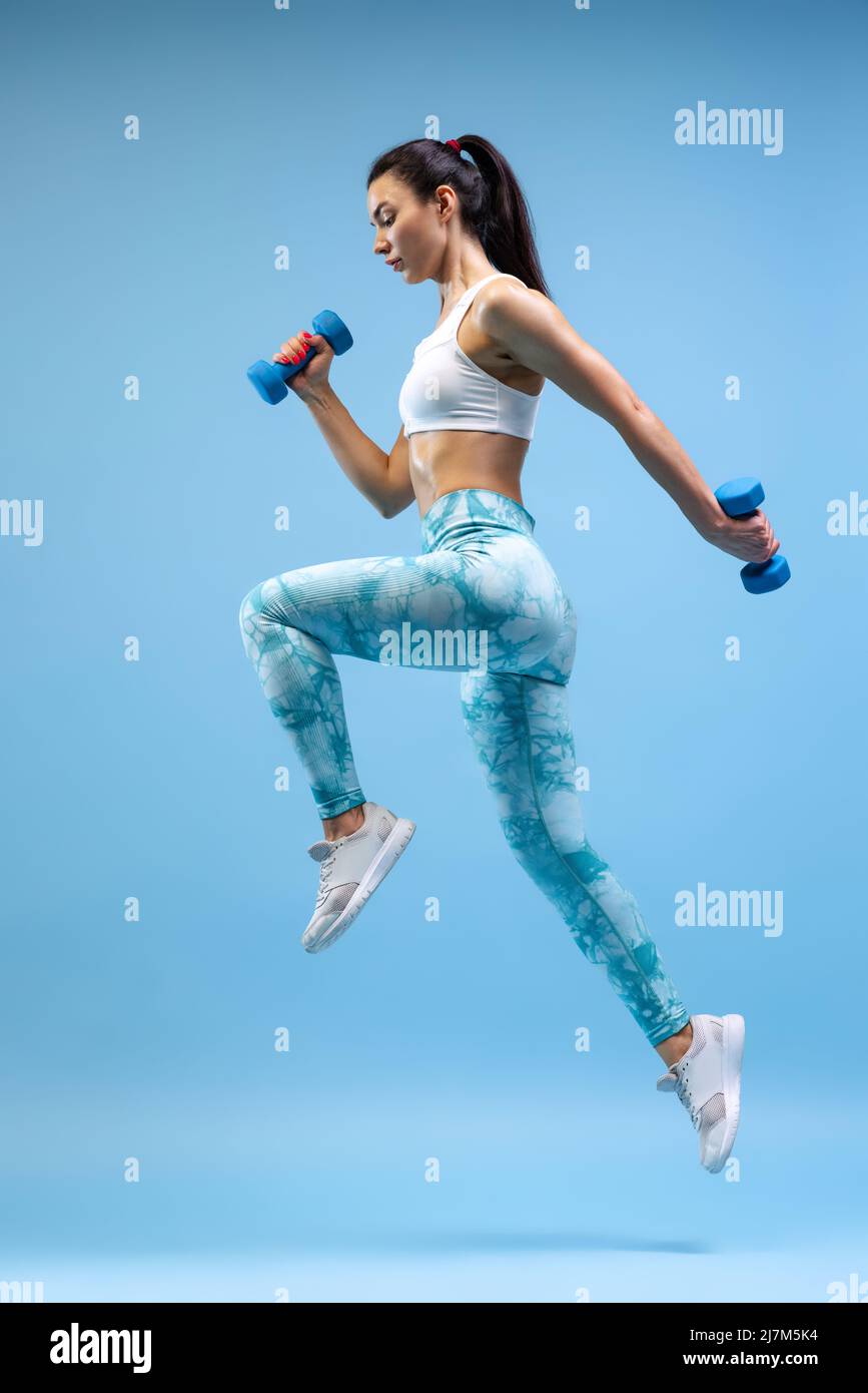 Full-length portrait of young sportive girl training, jumping with ...