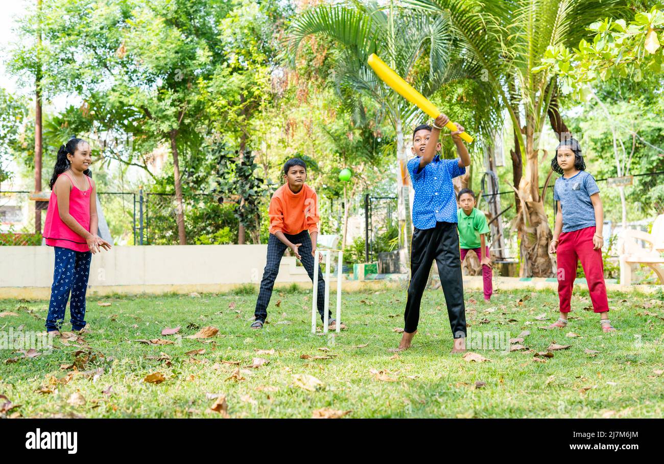 young kid running by hitting the ball while playing cricket at park for ...