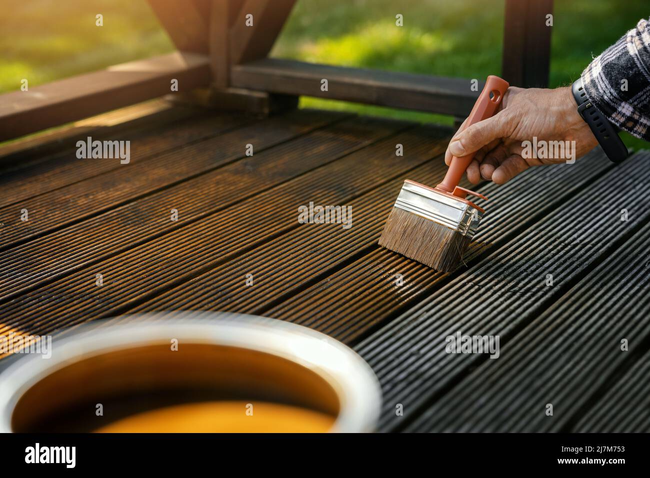 man applying brown wood protection oil on decking boards with paint ...