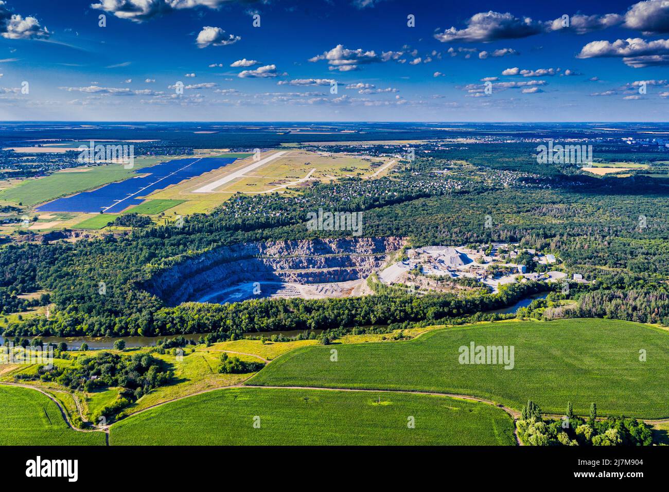 Top view of a stone, granite quarry. Beautiful forest, blue sky, clouds. River flows. Green ...