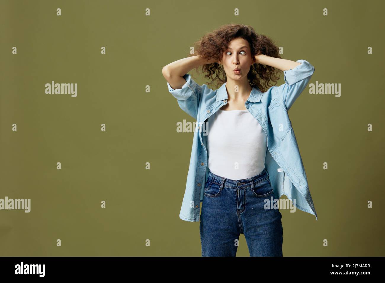 Cute funny curly beautiful lady in jeans shirt touches hair makes lips ...