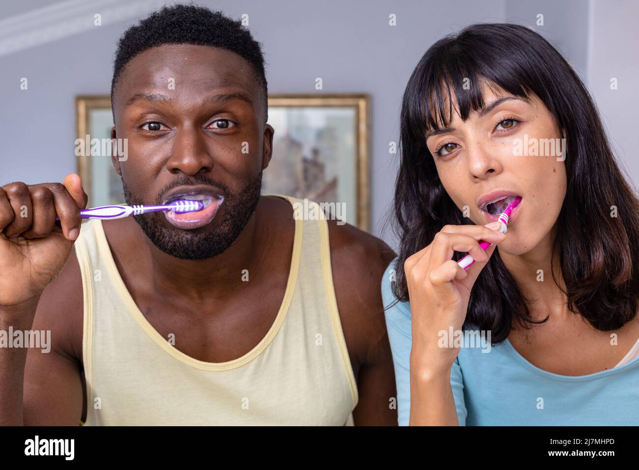 Portrait of multiracial young couple brushing teeth in bathroom at home ...