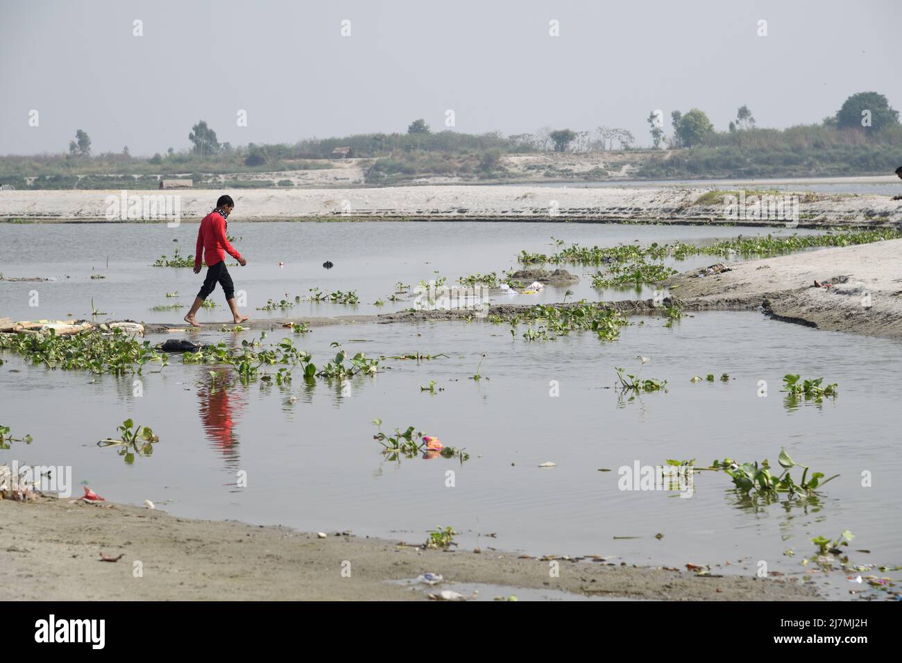 A man crossing low water in the shallow riverbed in the bank of the ...