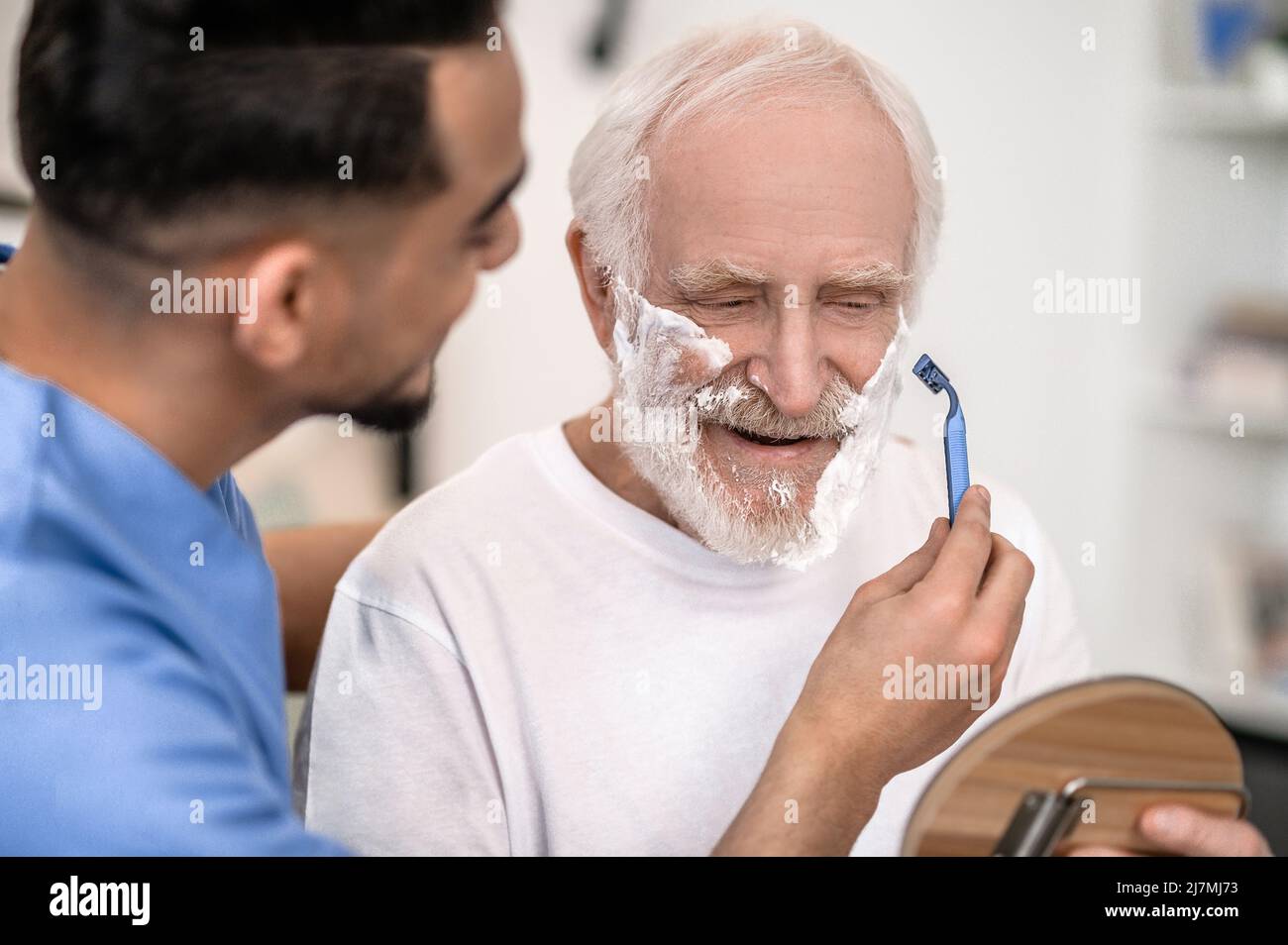 Caring volunteer giving a pleased old man a shave Stock Photo - Alamy