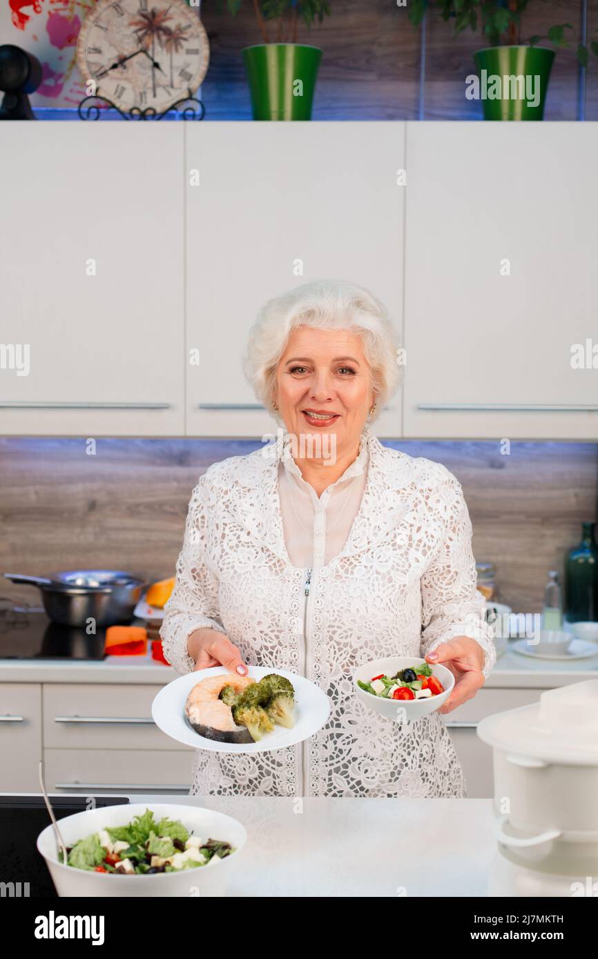 An older woman cooks in the kitchen, demonstrates cooked healthy food ...