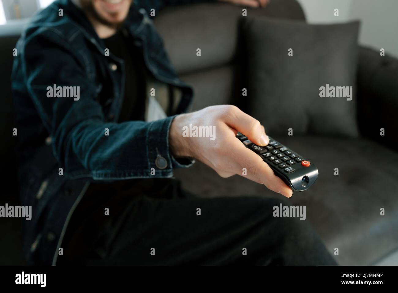 TV remote, young man sitting on sofa in living room changing channels ...