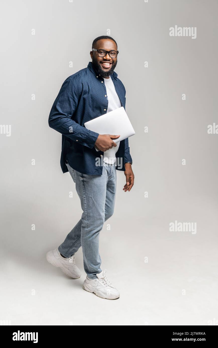 Cheerful African-American man carrying laptop computer isolated on grey ...
