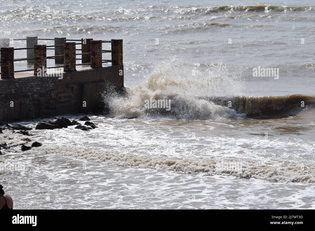big sea waves splashing against a pier. The pier cuts the sea waves off ...