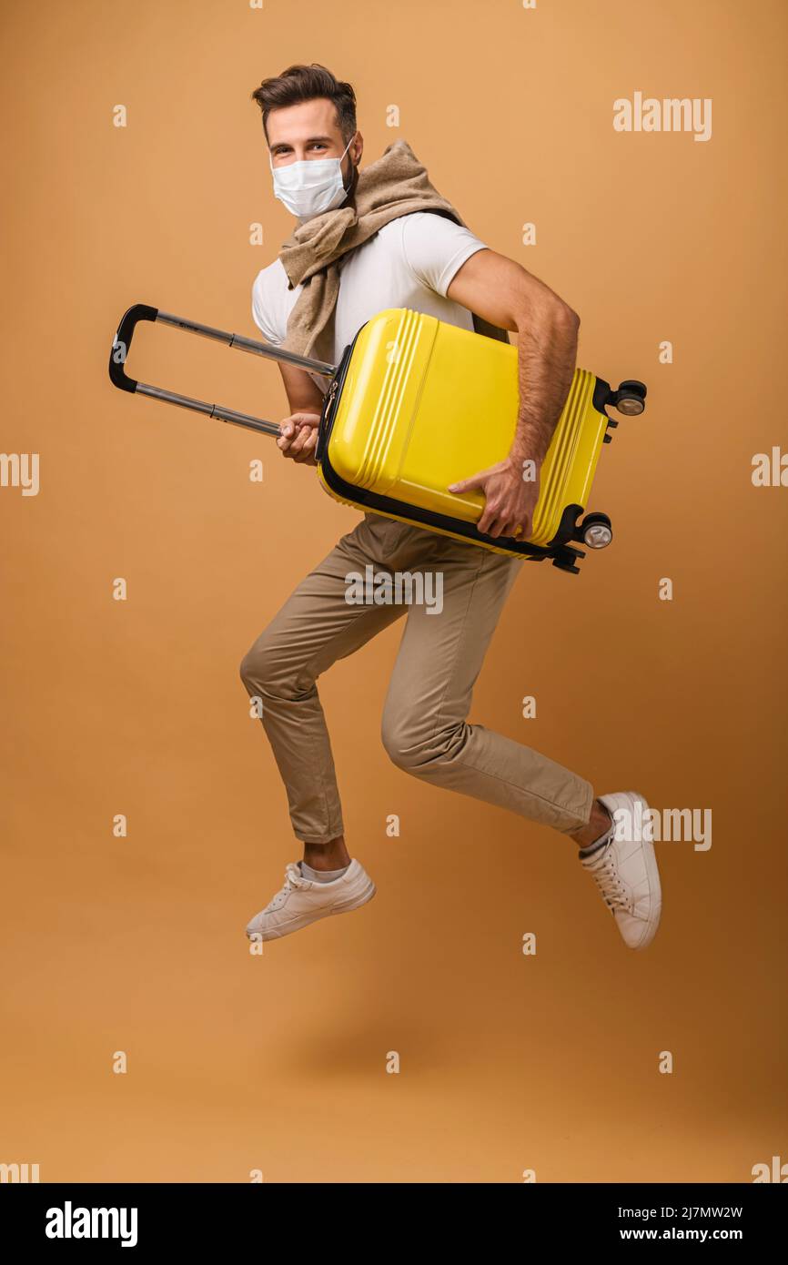 Joyful caucasian guy jumping with yellow suitcase, fooling around ...