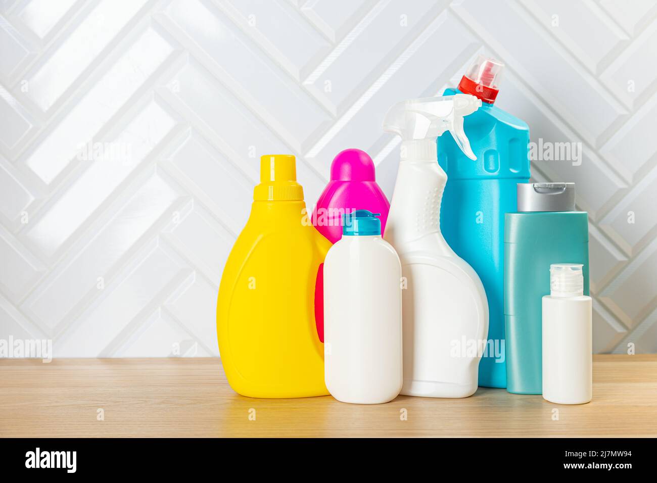 Bottles with detergent and cleaning supplies on wooden table and light ...