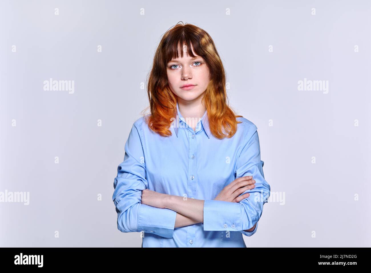 Studio portrait of serious sad young female looking at camera on light ...