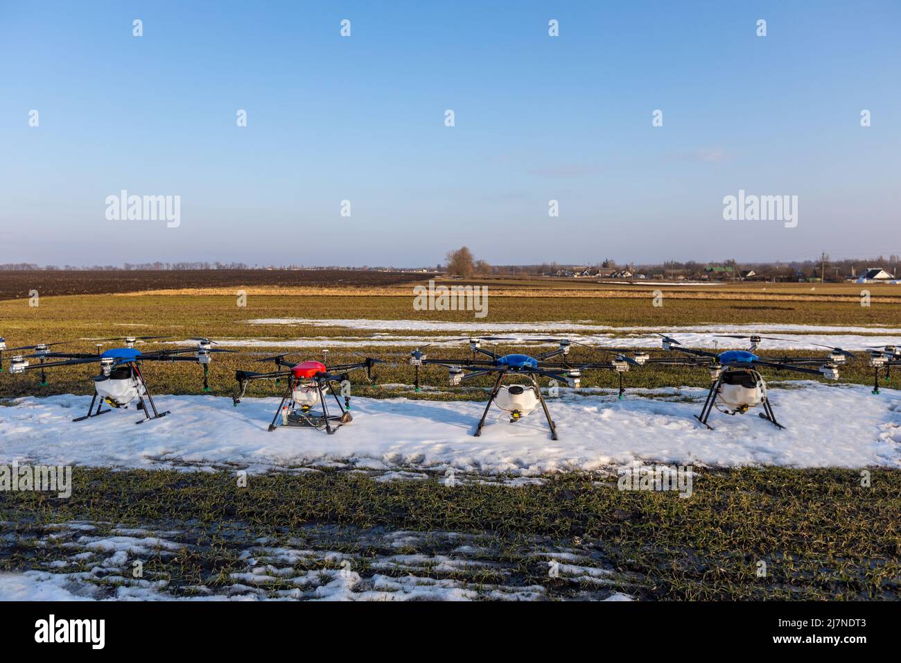 Many agrodrones are on the green field. The snow has not melted yet ...