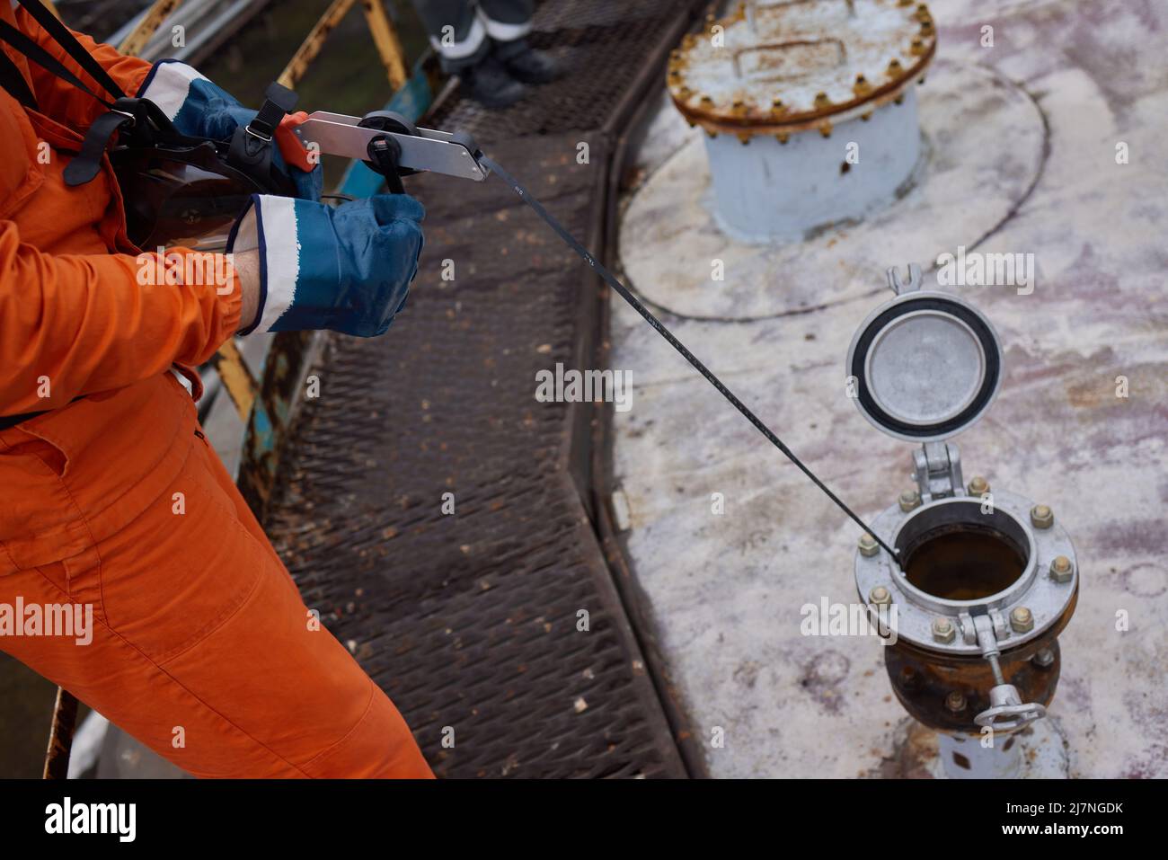 Young offshore engineer sounding fuel oil cargo tank on cargo deck on ...