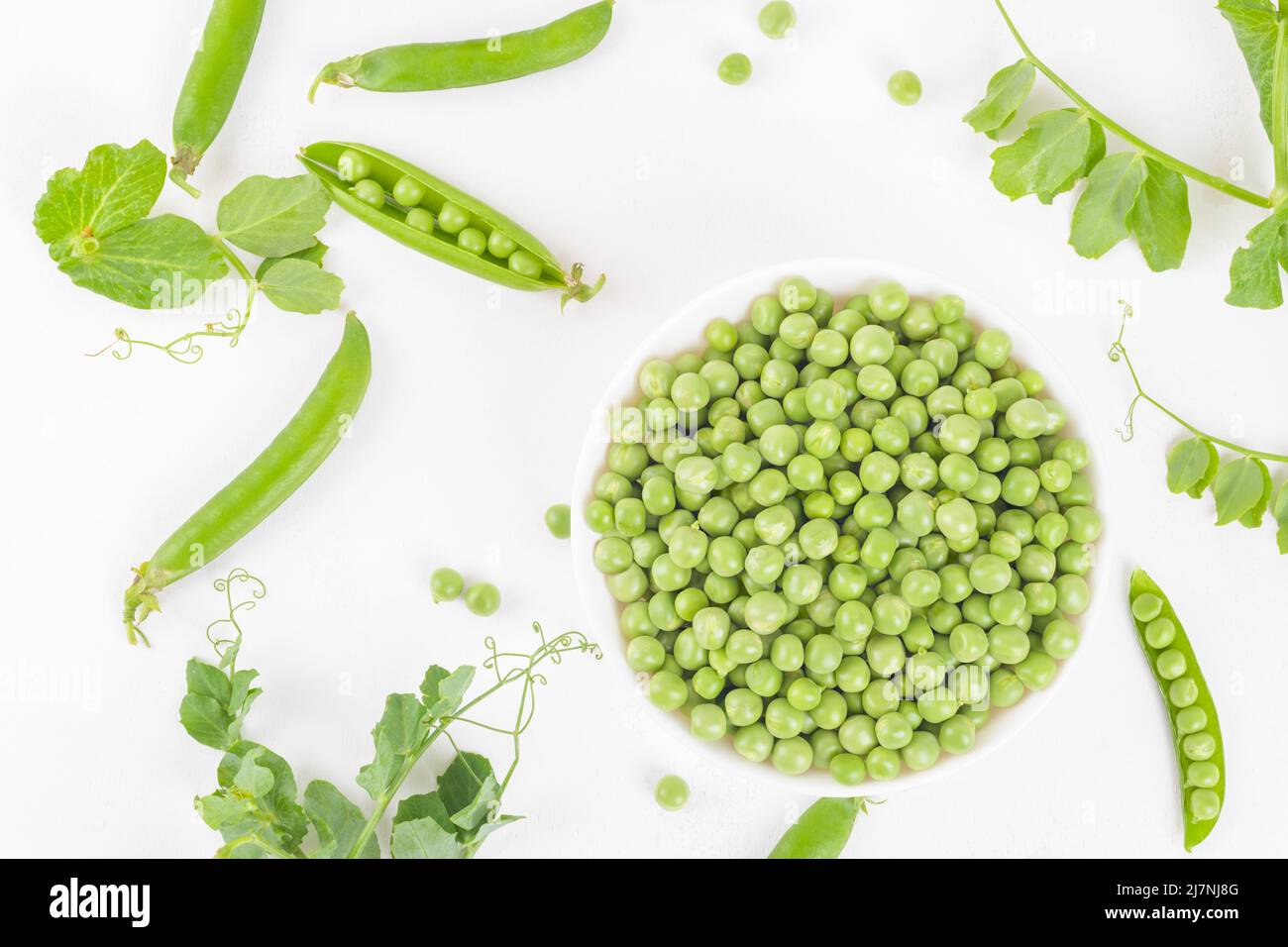 Fresh organic raw green peas in a bowl with peas pods and plants leaves ...