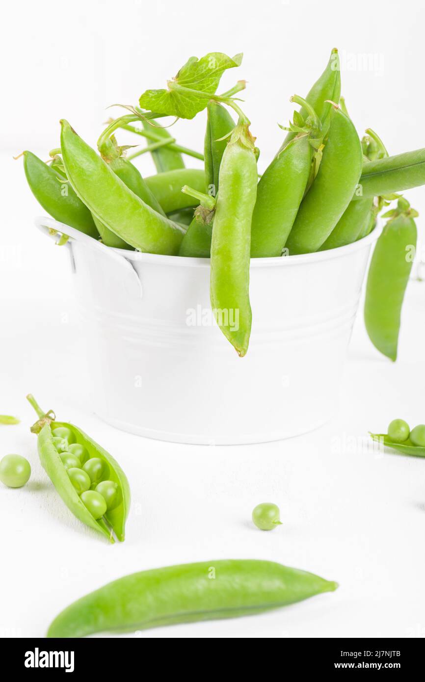Fresh organic raw green peas pods in a bowl and plants leaves on white ...