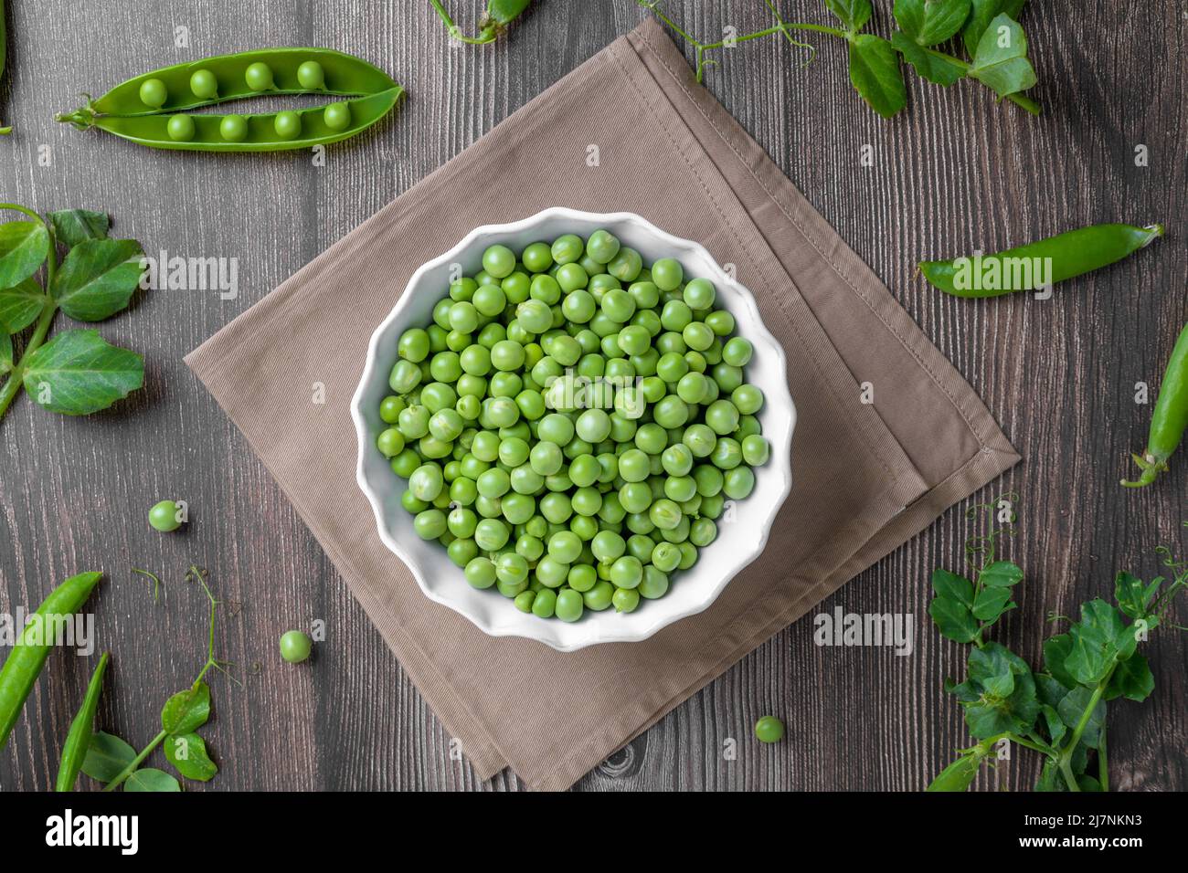 Fresh organic raw green peas in a bowl with peas plants leaves on dark ...