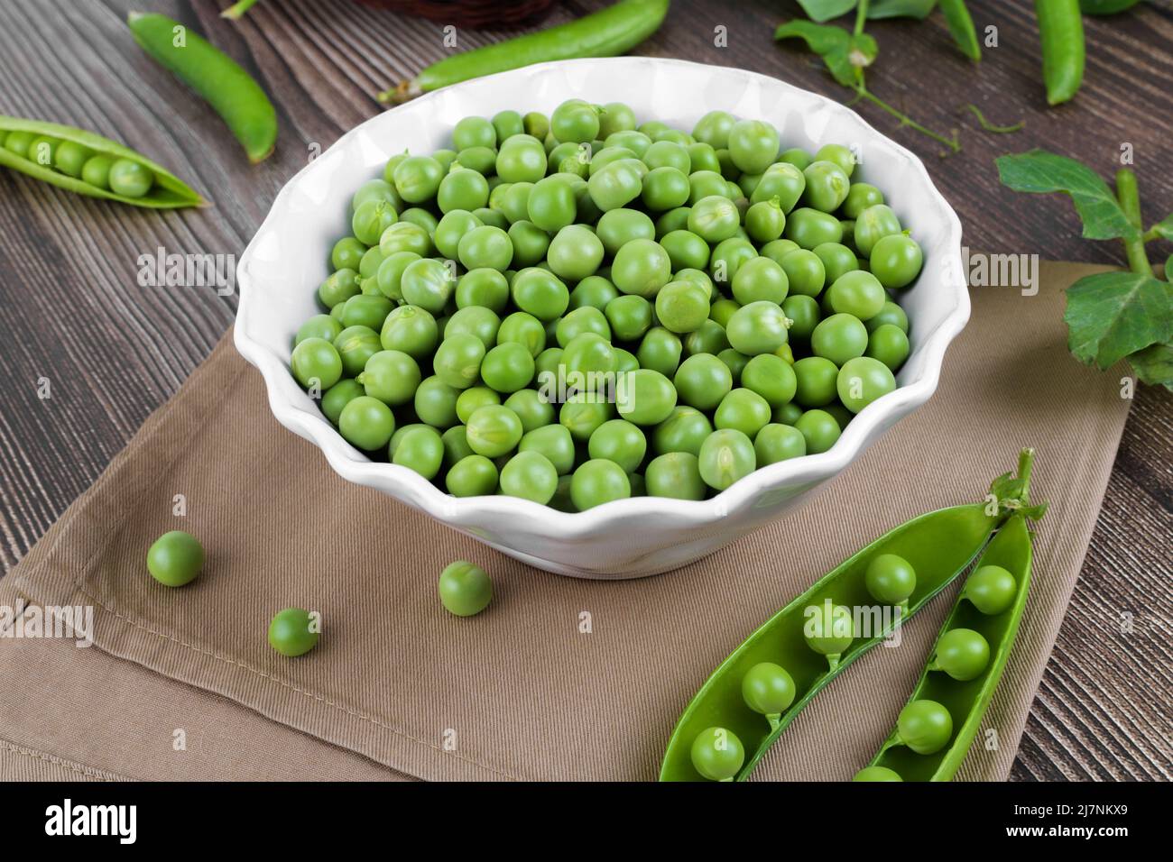 Fresh organic raw green peas in a bowl with peas plants leaves on dark ...