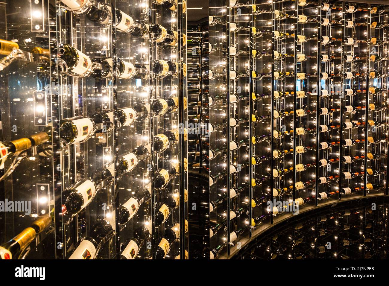 A wall of wine bottles of various types in a curved glass wall, making ...