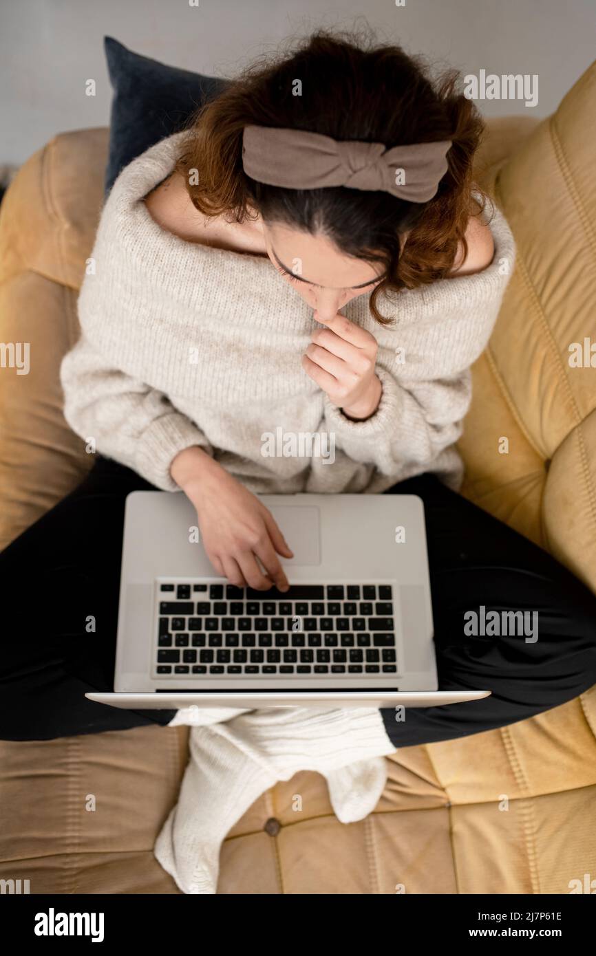 top view of young woman cross-legged sitting on sofa working on laptop ...