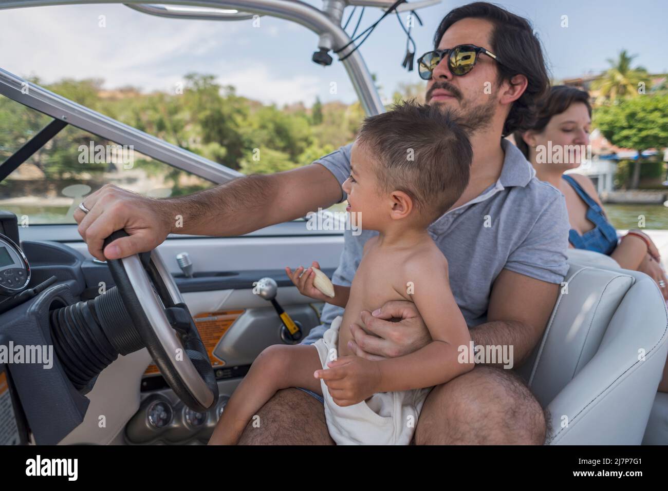 Young father carrying his son sailing steering a boat sitting Stock ...