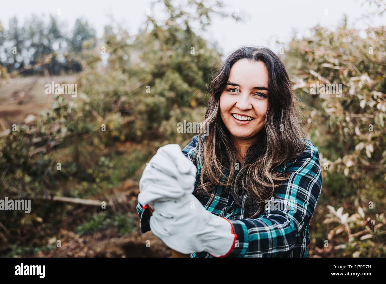 Medium shot of a smiling latin peasant woman using gardening gloves and ...