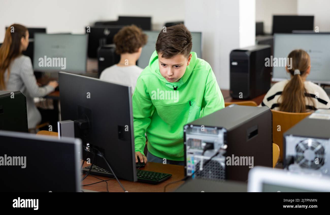 Schoolboy using computer at lesson, teacher teaching pupils in class ...