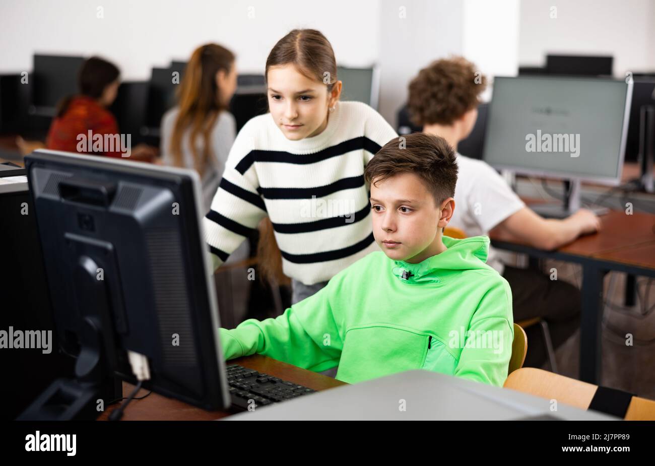 Teen girl talking to concentrated teenager studying in computer lab ...