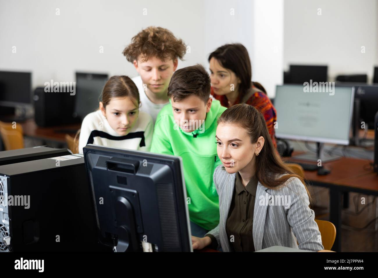 Female teacher and teen students looking at monitor screen during ...