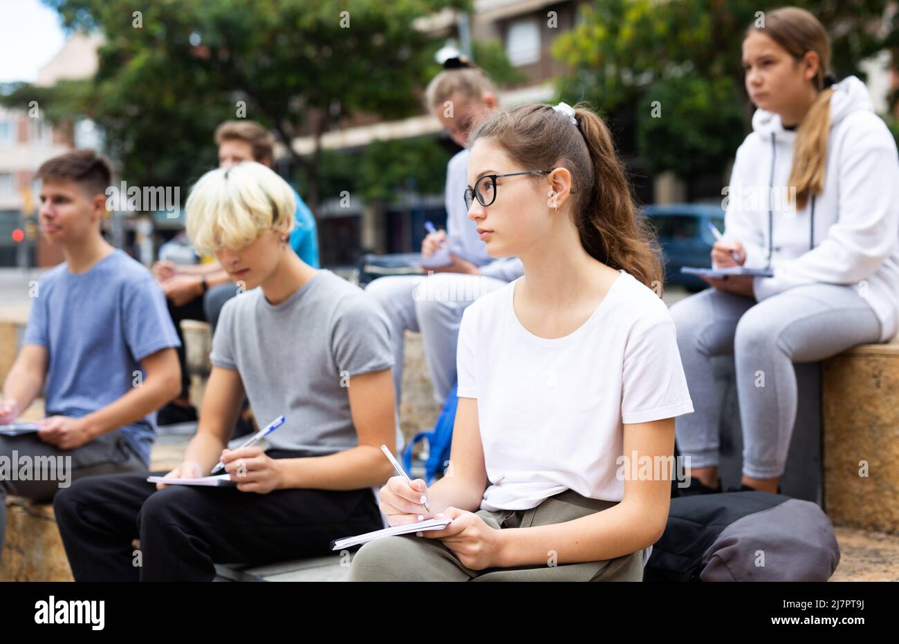 Attentive students write lesson in a notebook sitting on stone street parapet Stock Photo - Alamy