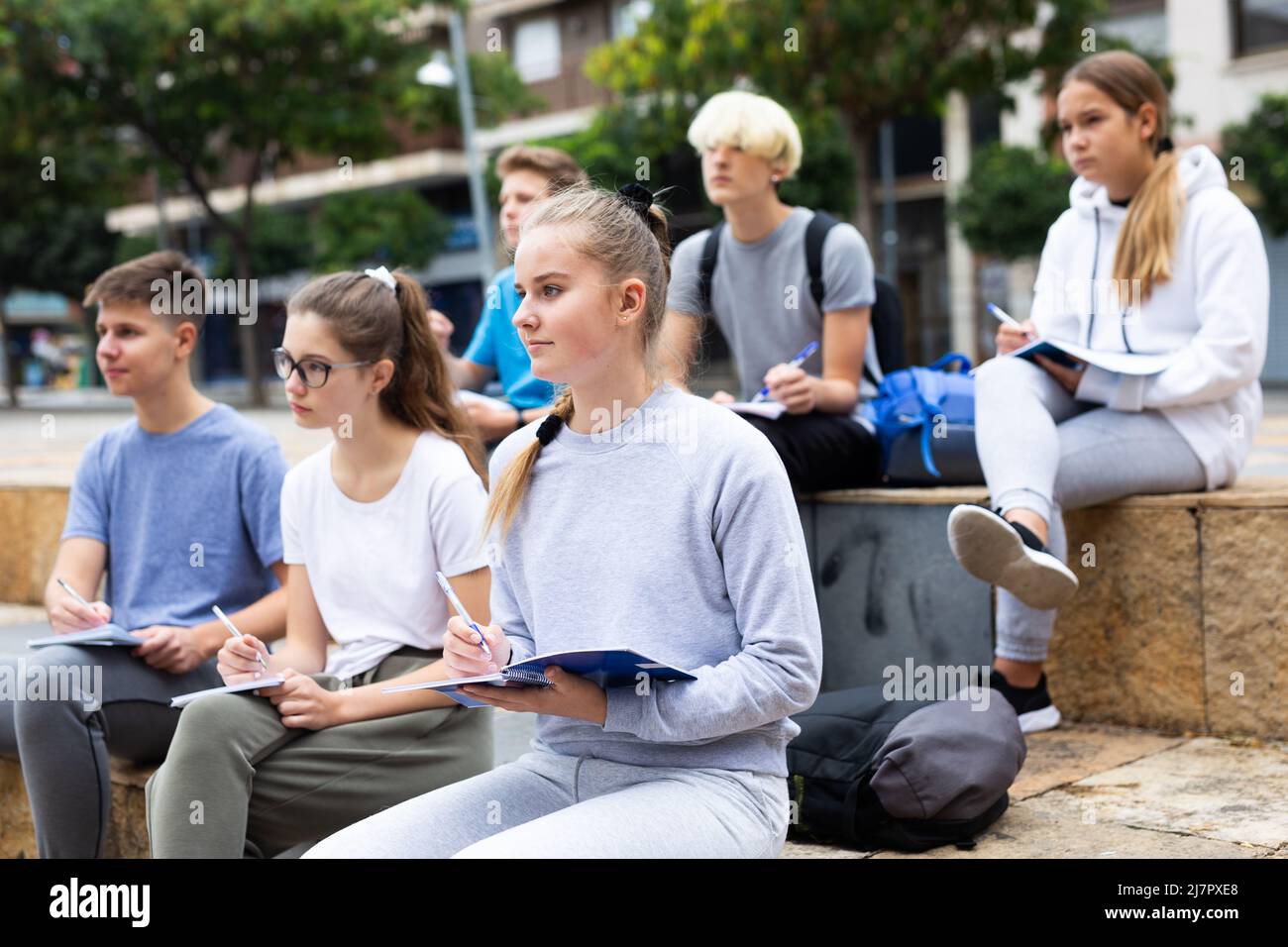 Attentive students write lesson in a notebook sitting on stone street parapet Stock Photo - Alamy