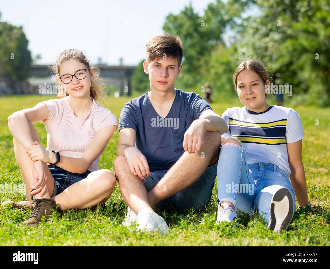Three happy teenagers sitting on green lawn Stock Photo - Alamy