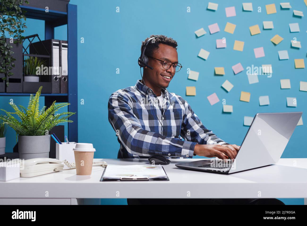 Helpline support agent wearing headset and using work computer while ...