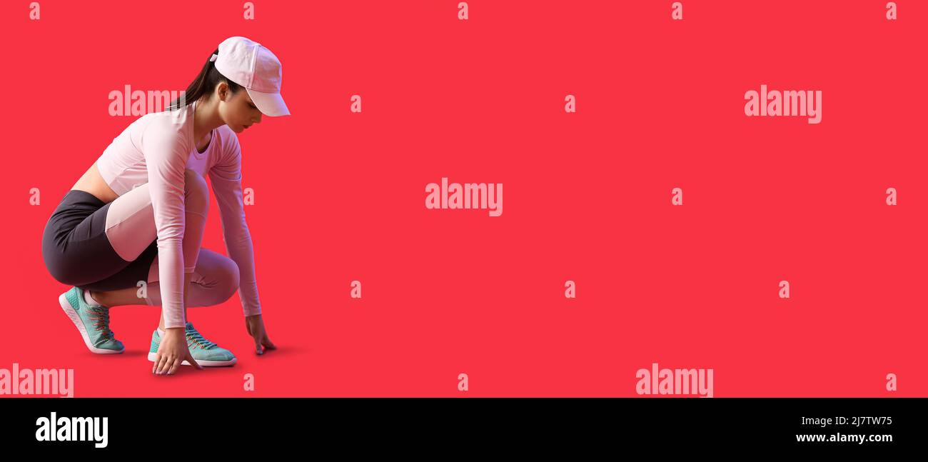 Sporty female runner in crouch start position on red background with ...
