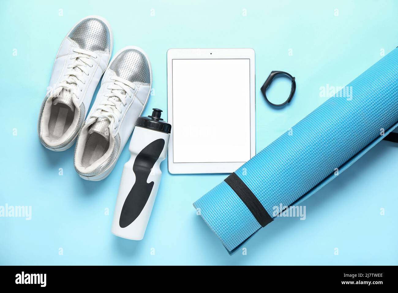 Tablet computer with shoes, bottle, smartwatch and mat on blue ...