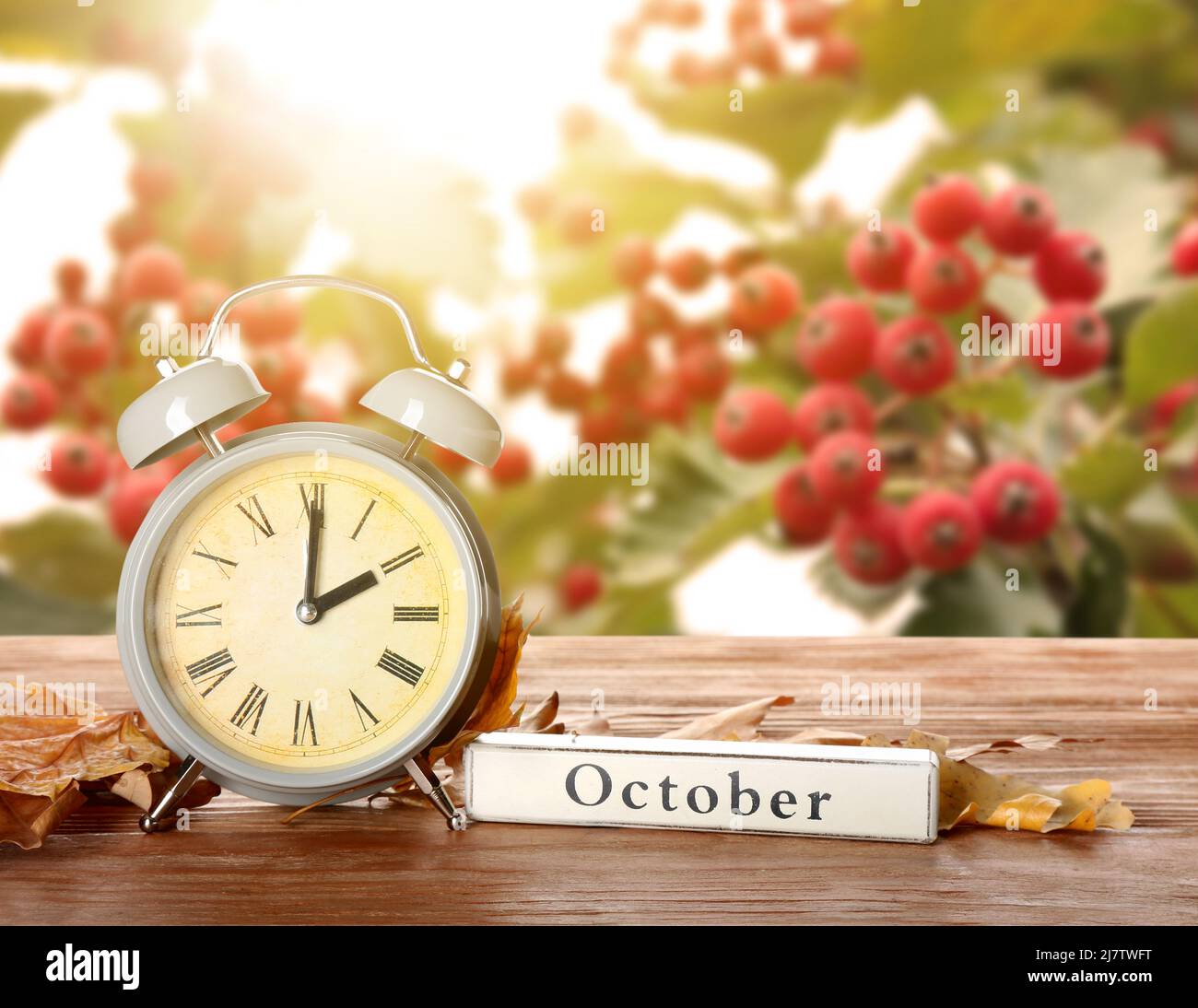 Alarm clock, word OCTOBER and autumn leaves on table outdoors. Daylight ...