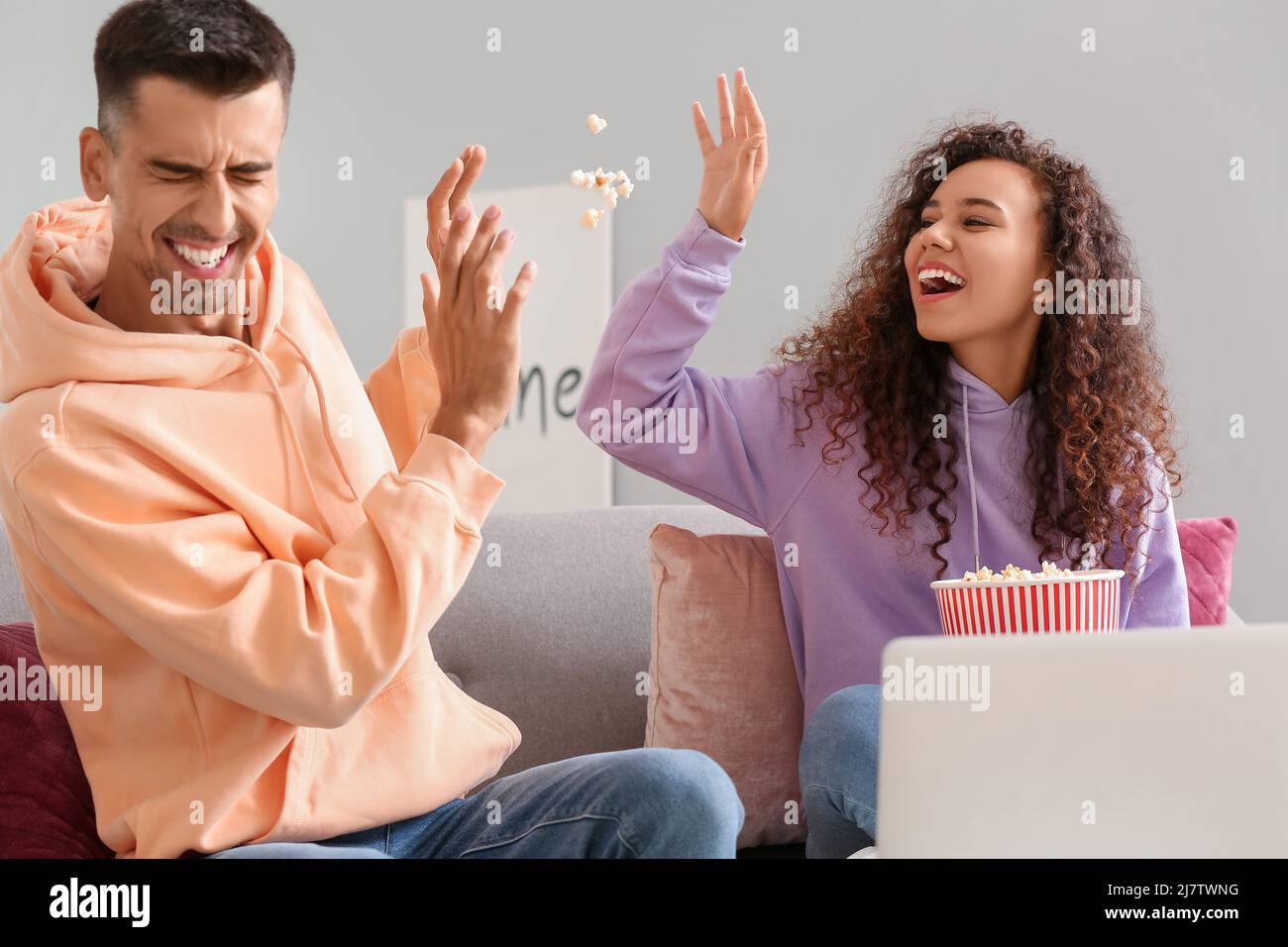Young woman throwing popcorn at her boyfriend while watching movie at ...
