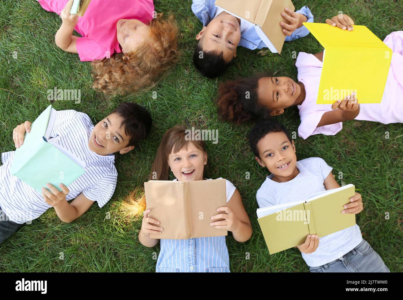 Little children with books lying on green grass in park Stock Photo - Alamy