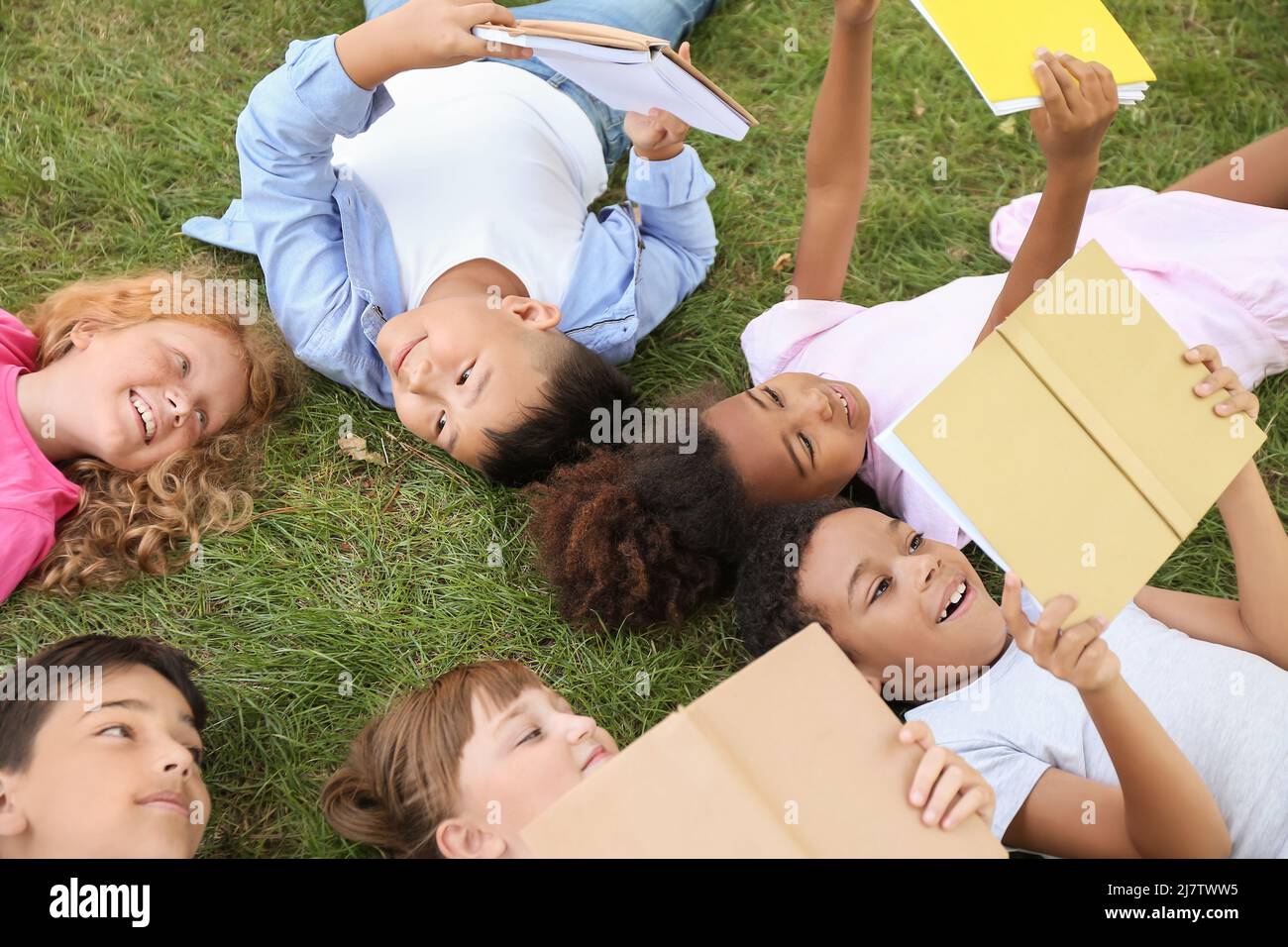 Little children with books lying on green grass in park Stock Photo - Alamy