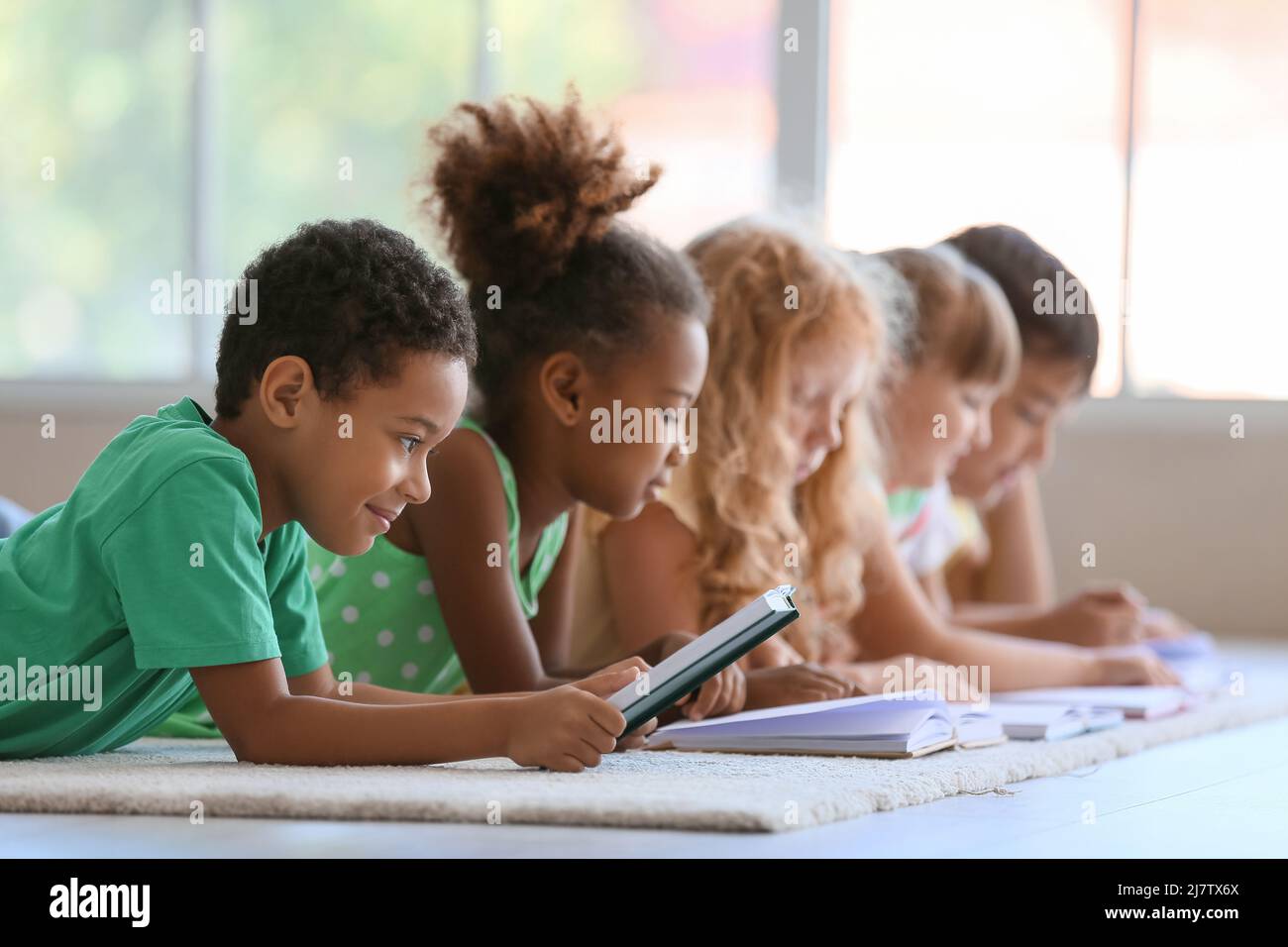 Cute little children reading books on floor in classroom Stock Photo ...