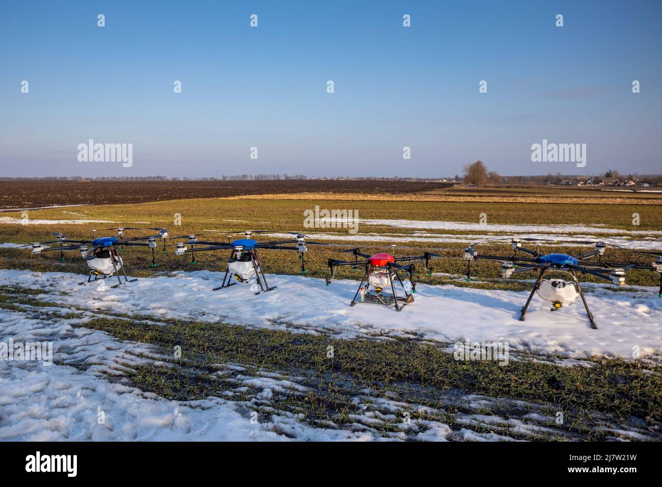 Many agrodrones are on the green field. The snow has not melted yet ...