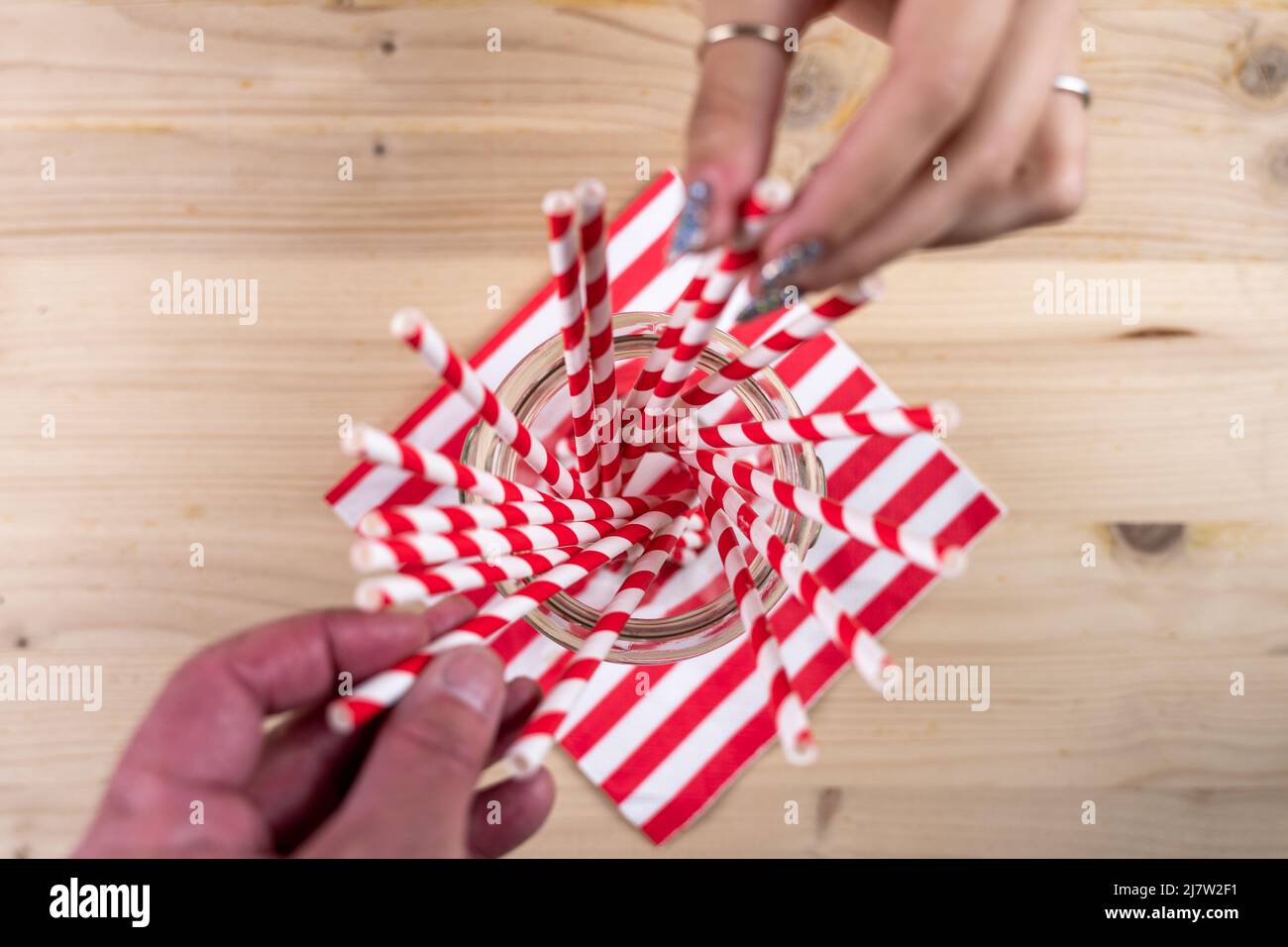 close-up of a lot of straws in a glass cup on a wooden table - hands ...