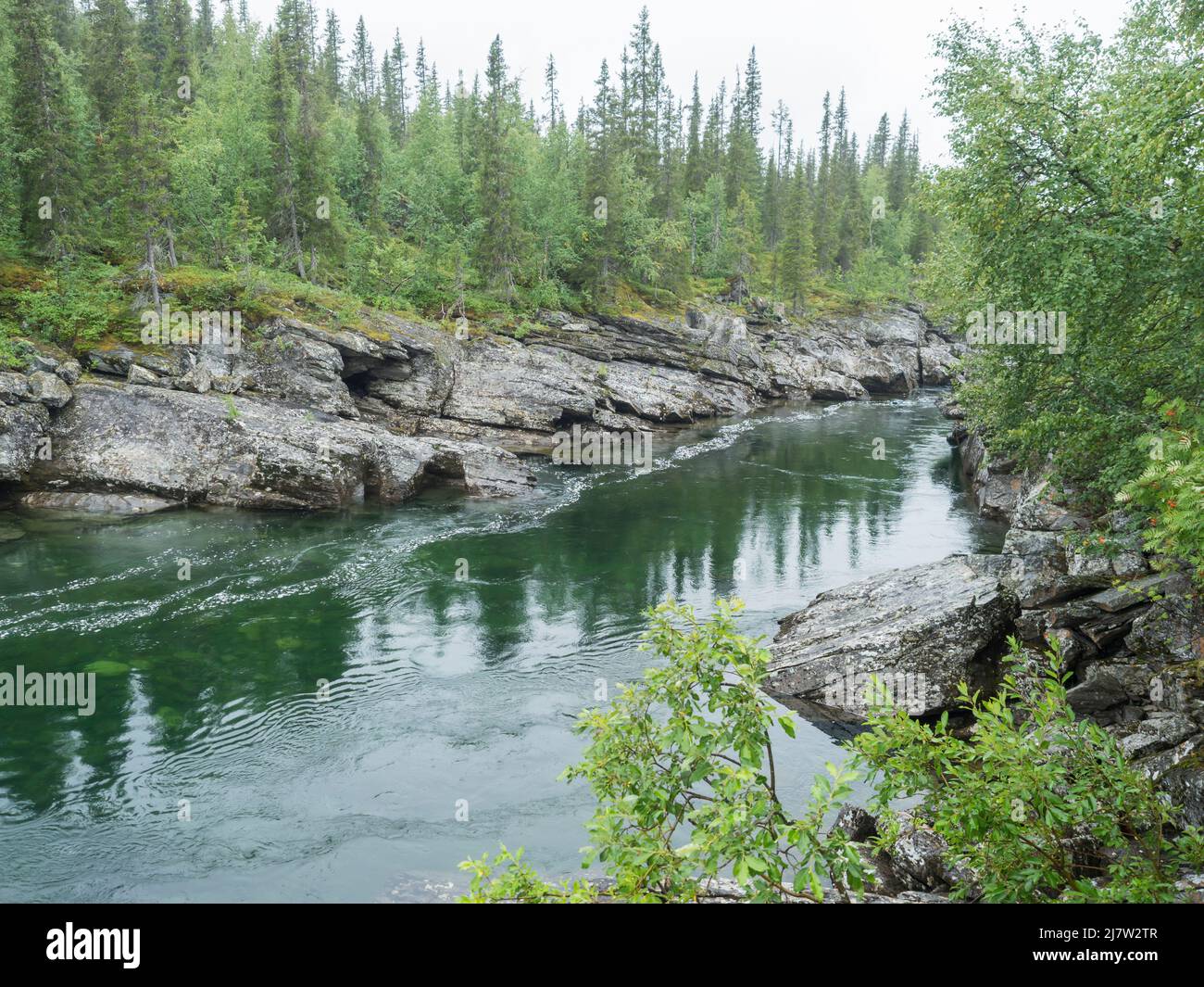 View of winding Tarra river with birch bush, gravel, grass and granite ...