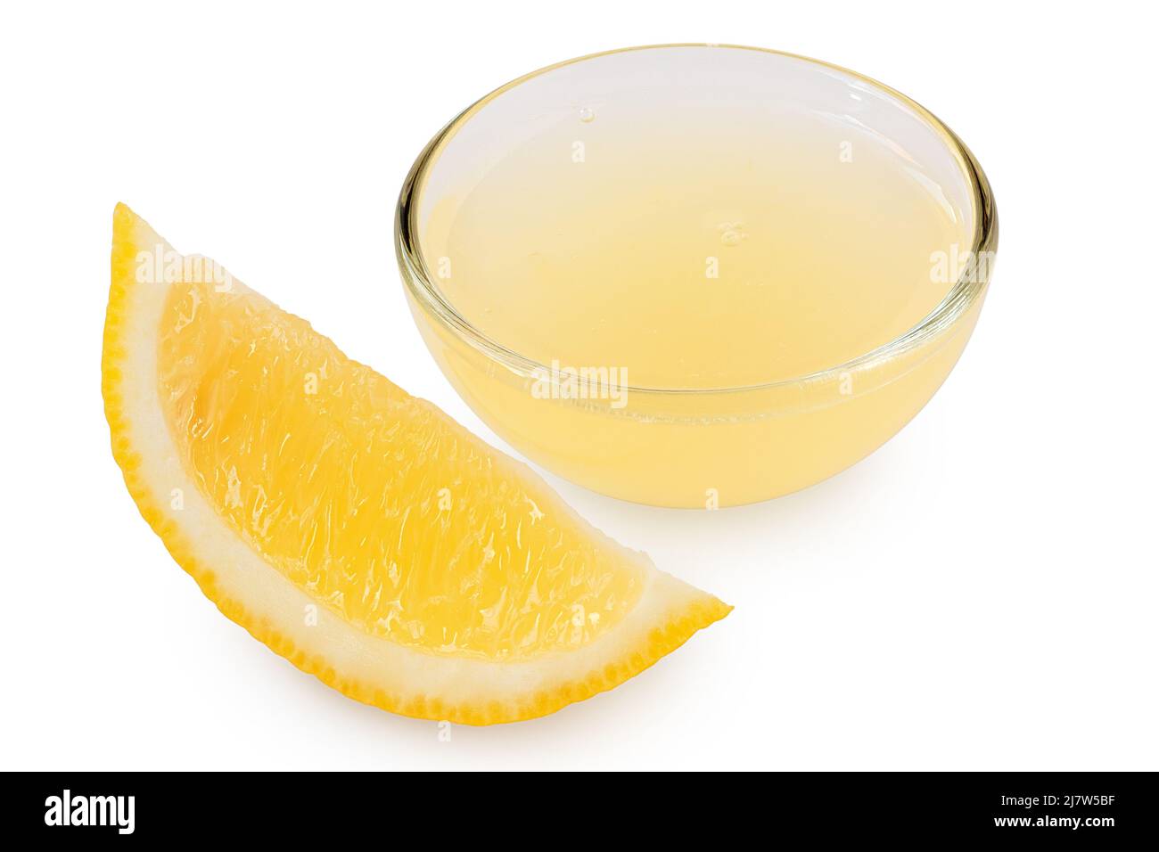 Freshly squeezed lemon juice in a glass bowl next to lemon segment ...