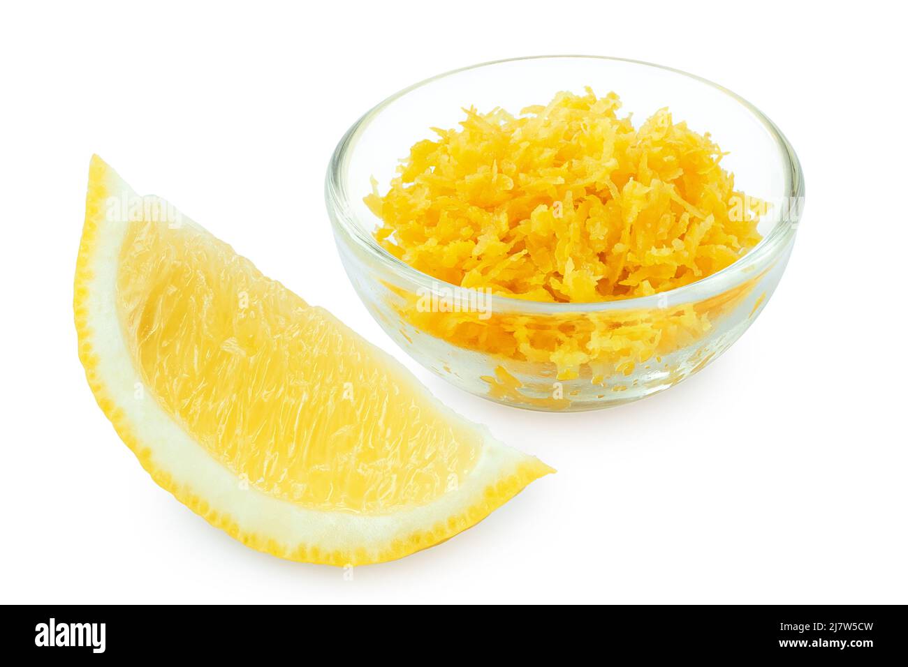 Freshly grated lemon zest in a glass bowl next to lemon segment ...