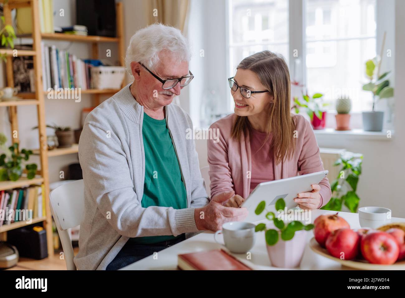 Adult daughter visiting her senior father at home and using tablet ...