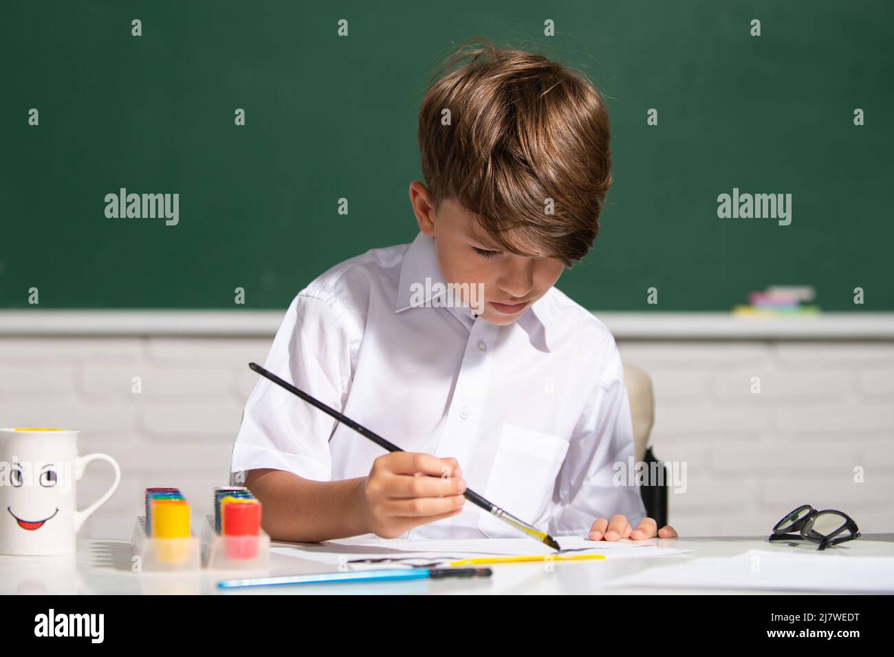 Cute little child drawing in classroom. Portrait of school boy enjoying ...